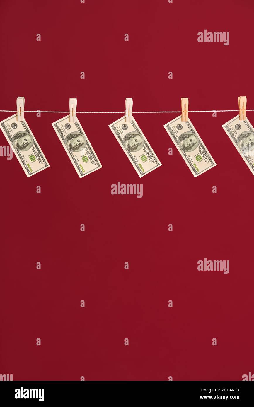 Money laundering, US dollars hanging on rope over red studio background ...