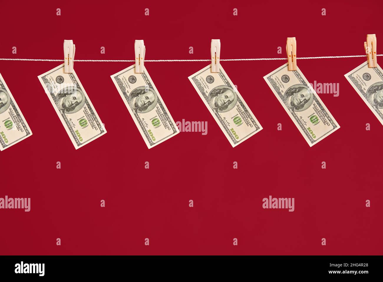 Money laundering, US dollars hanging on rope over red studio background ...