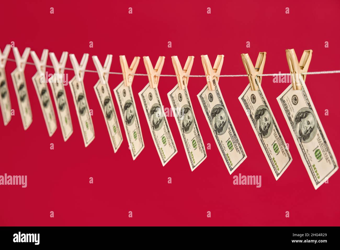 Money laundering, US dollars hanging on rope over red studio background ...