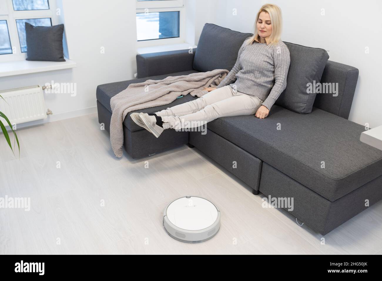 Robotic vacuum cleaner cleaning the room while woman resting on sofa ...