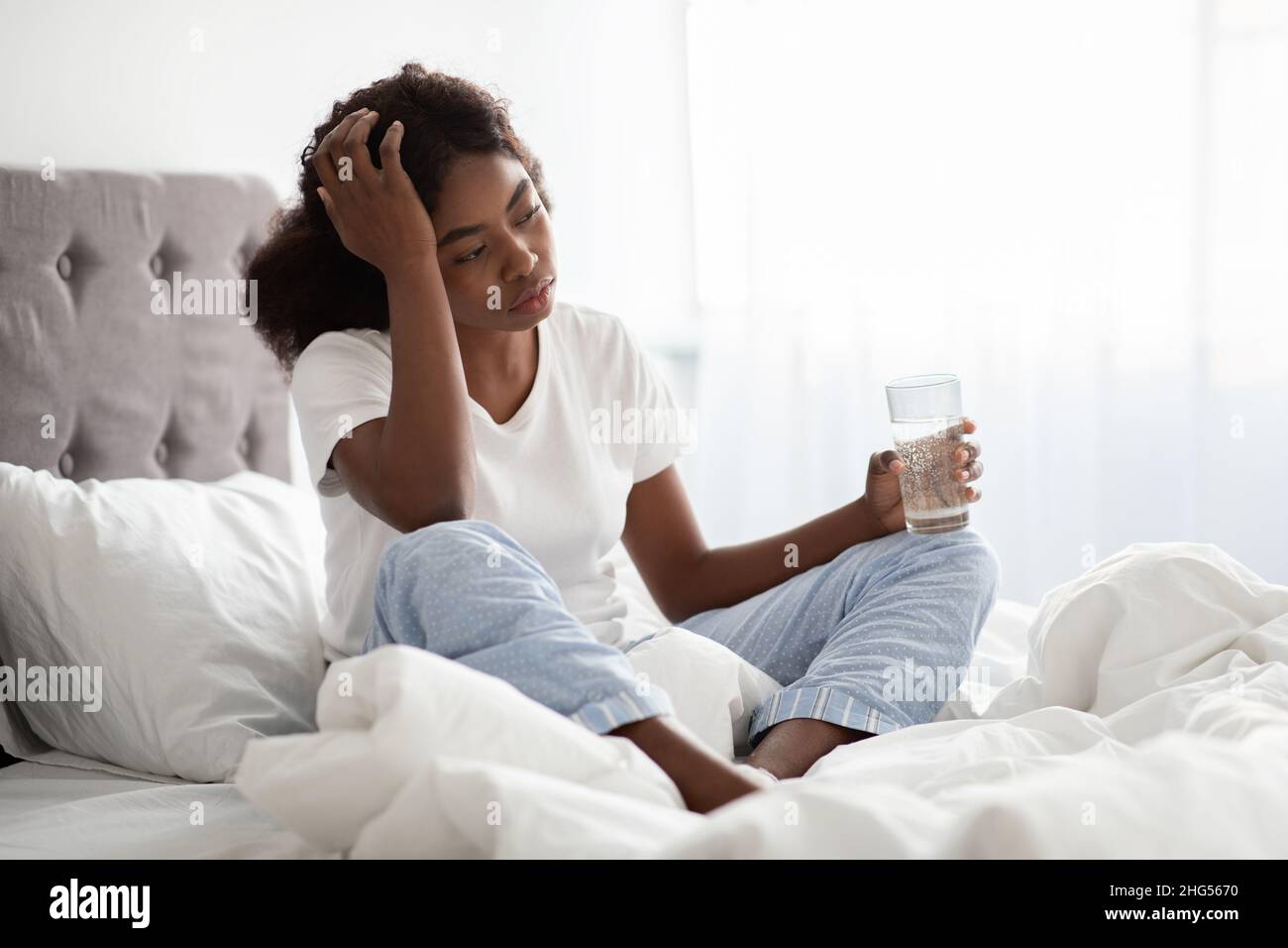 Sick african american lady feeling bad, touching head, bedroom interior ...