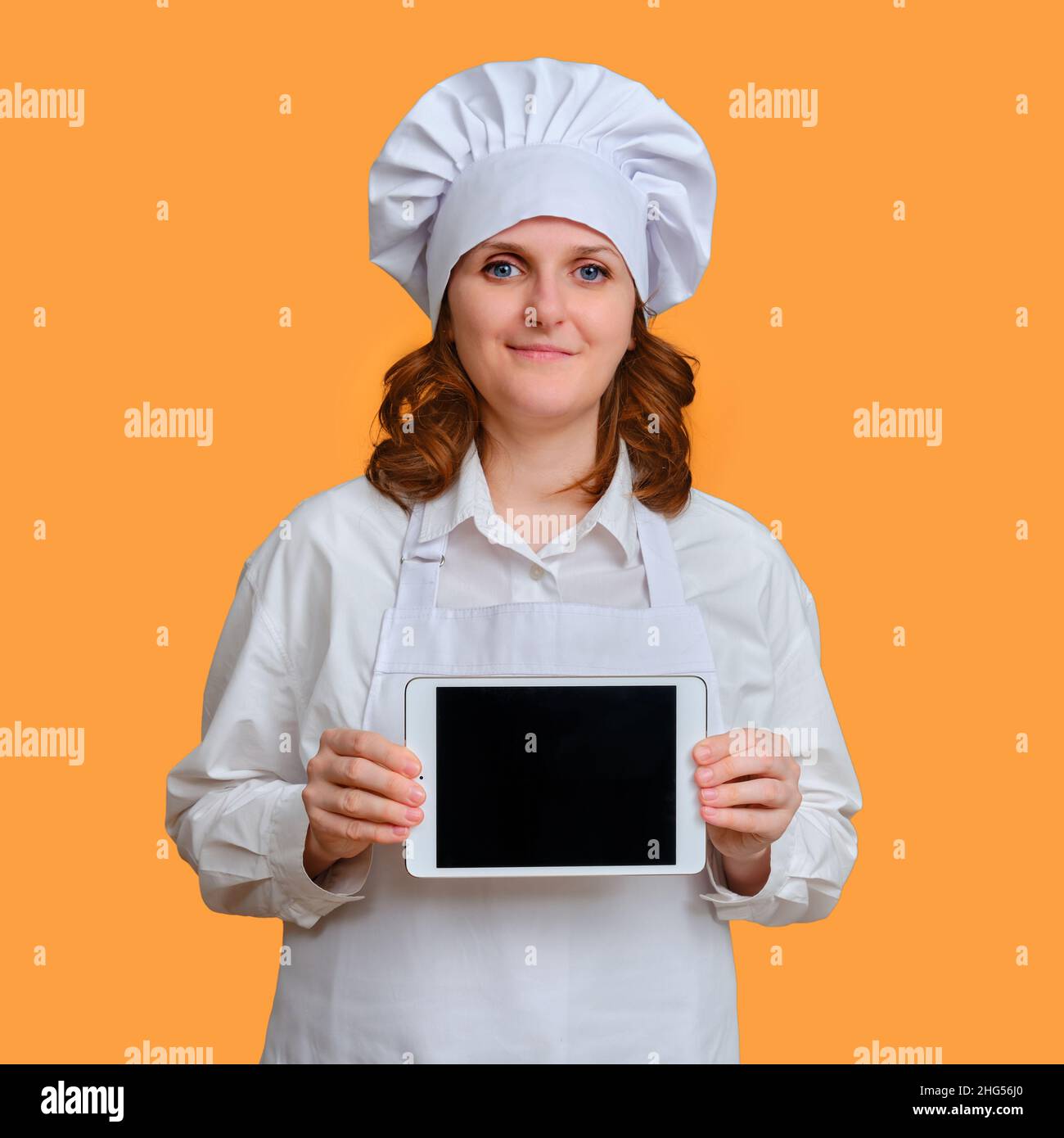 Happy woman chef showing tablet screen on yellow studio background ...