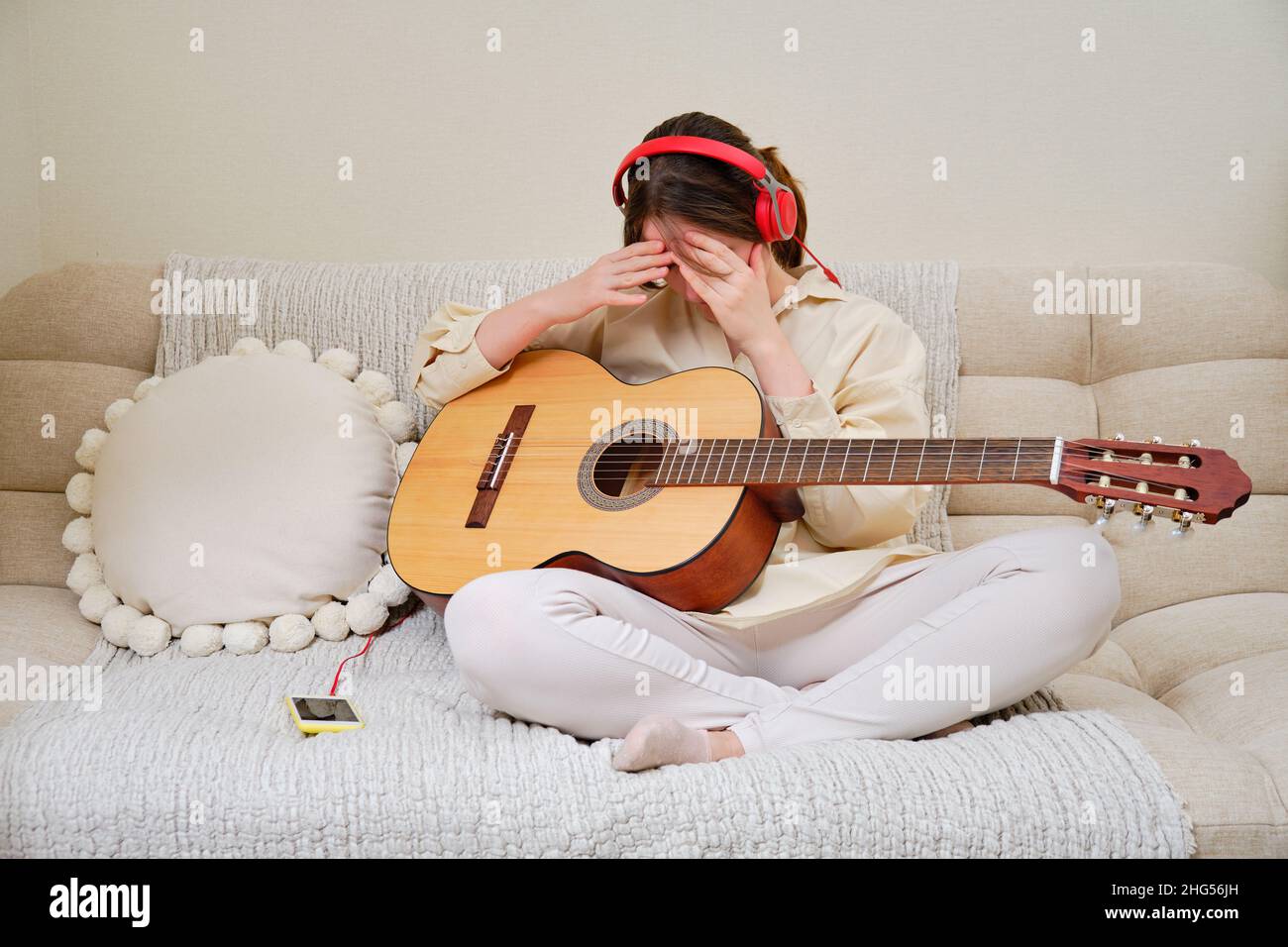 A shamed crying woman with acoustic guitar sitting on a bed in a home ...
