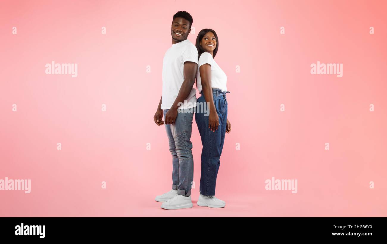 Confident couple standing back to back at pink studio background Stock ...