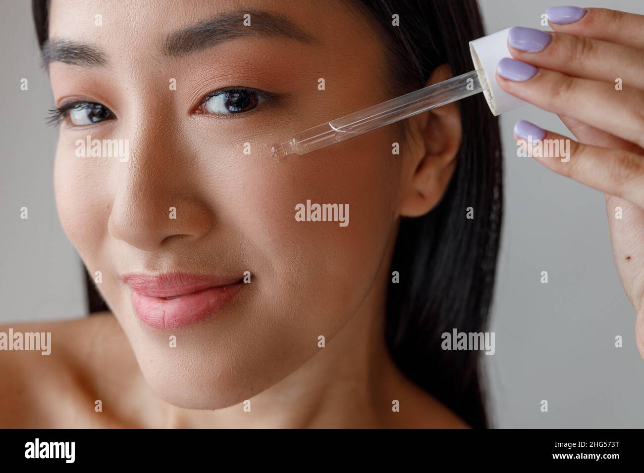 Smiling young woman applying vitamin serum on her face Stock Photo - Alamy