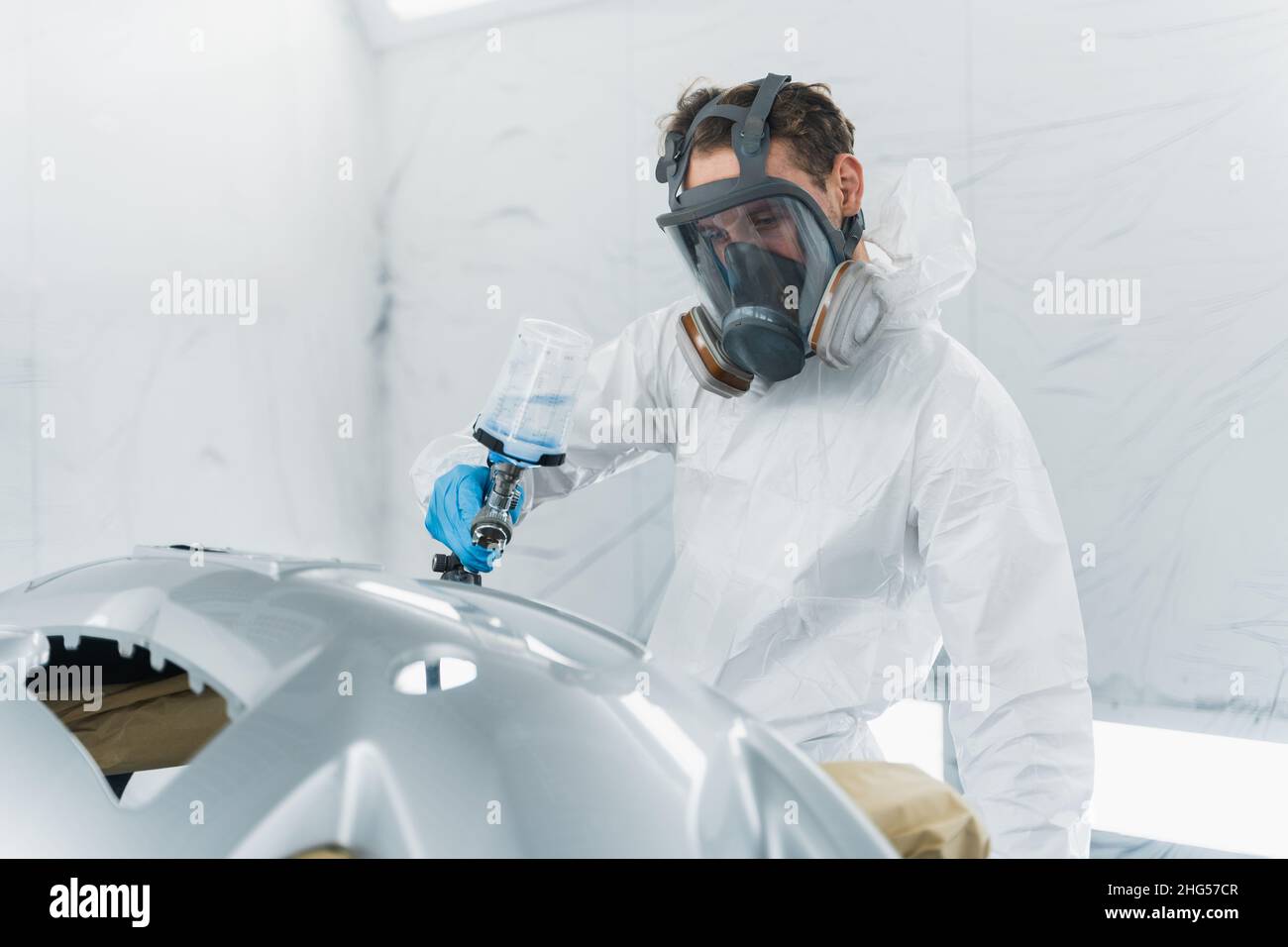 Auto painter varnishing a car body part in a painting booth. Repairman ...