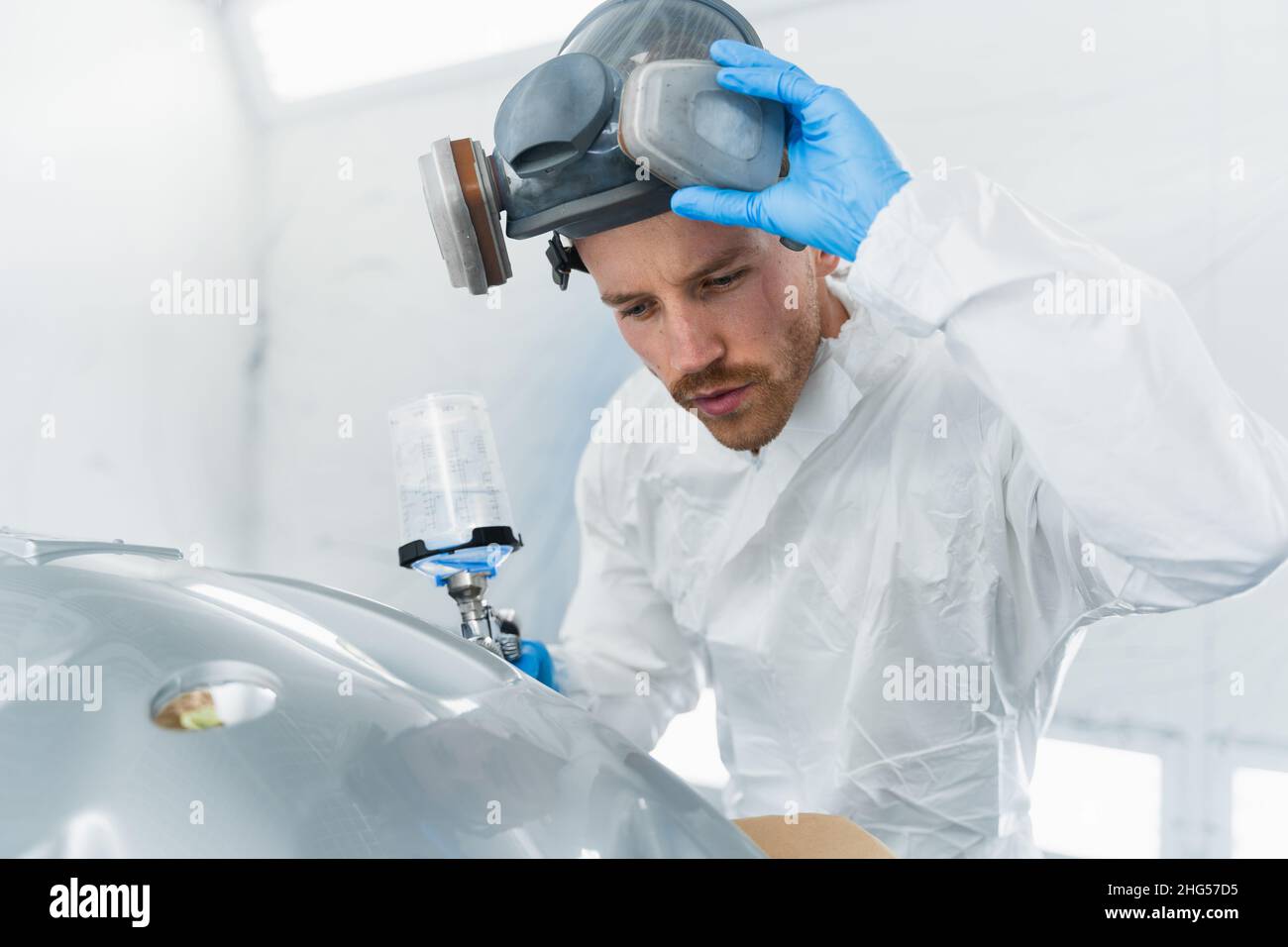 Professional car painter in the painting booth takes off his protective ...