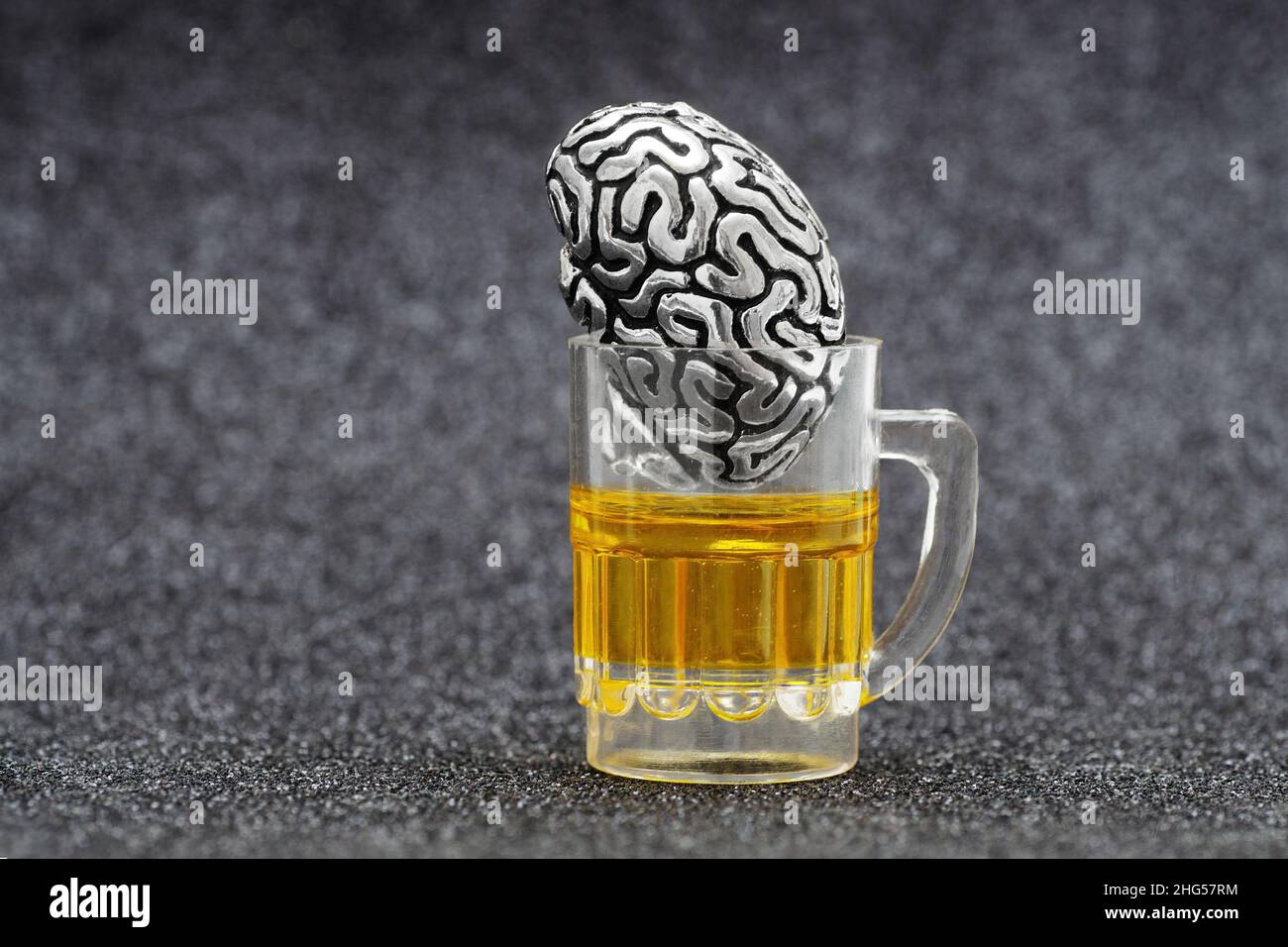 Anatomical copy of a human brain in a miniature beer mug against a gray ...