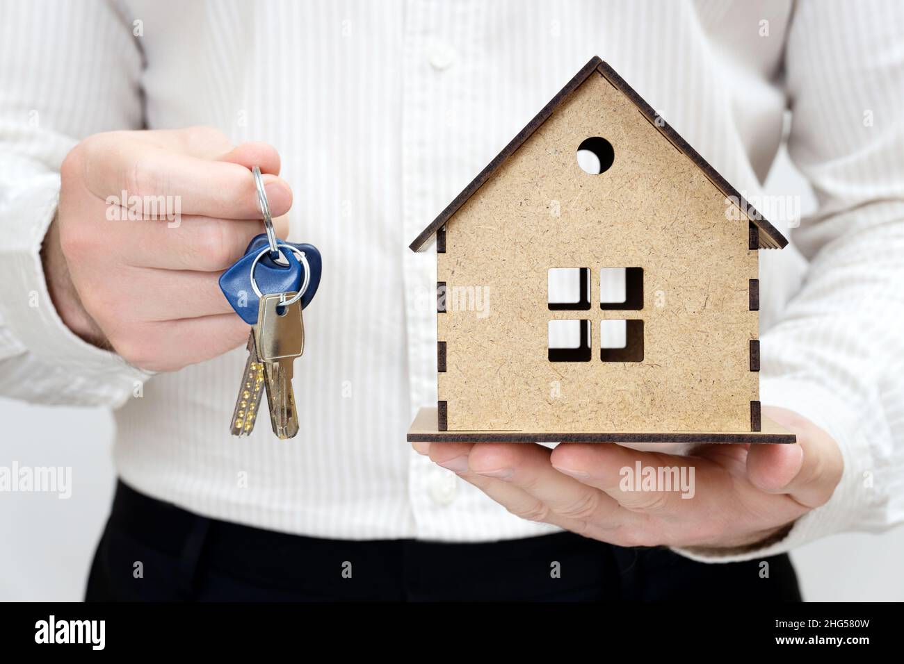 Man holding keys and a miniature wooden house model in hands. Get the ...