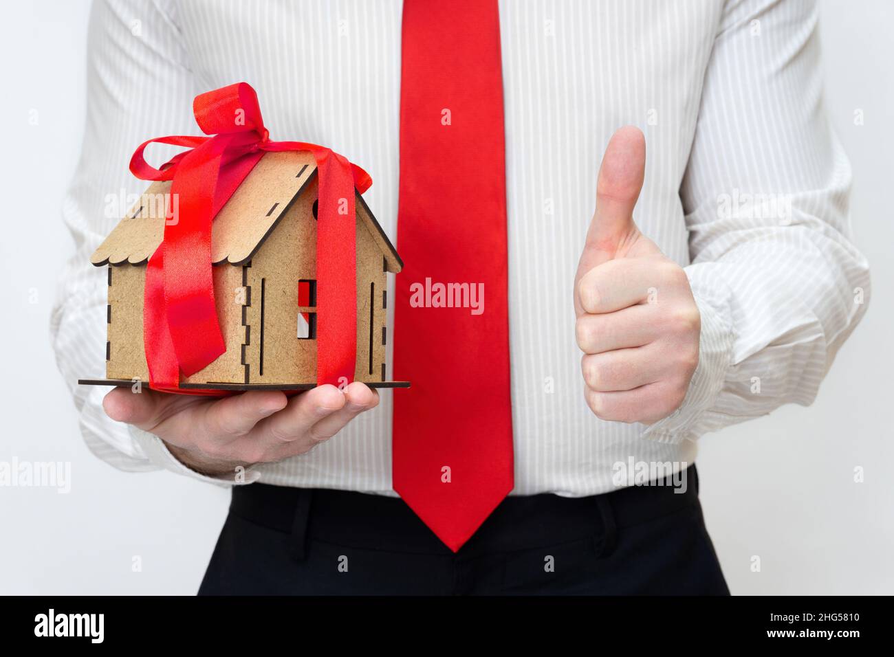 Businessman holding a miniature house model wrapped with a red ribbon ...
