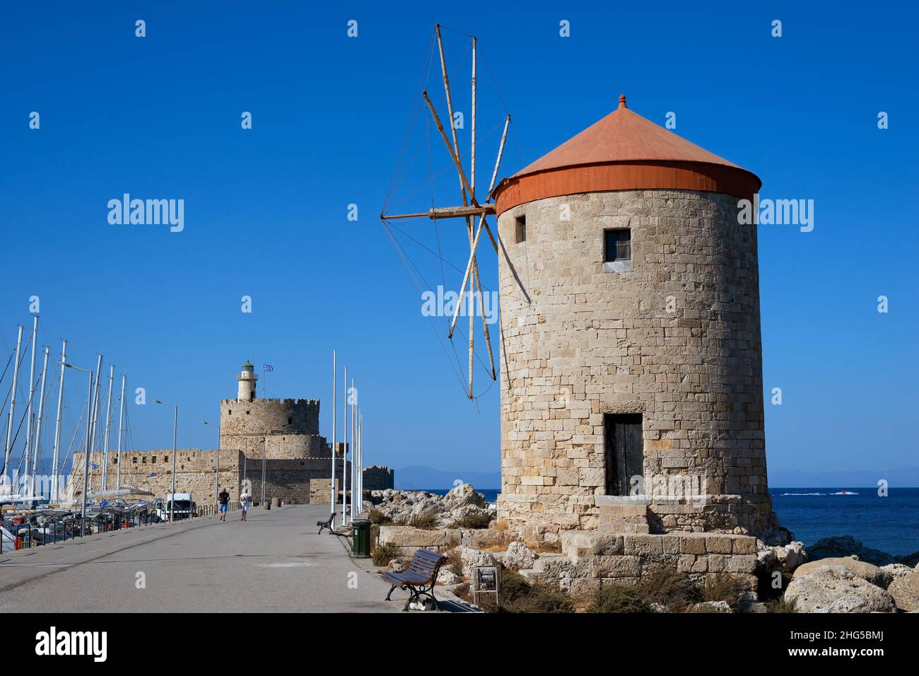 Windmill in Rhodes Mandraki harbour during sunny day against blue sky ...