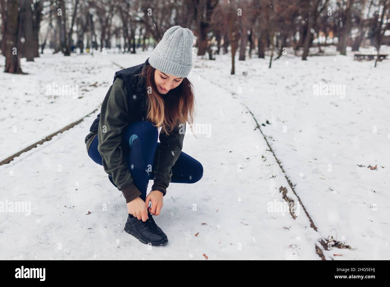 Runner tying shoe laces in snowy winter park. Woman training working ...