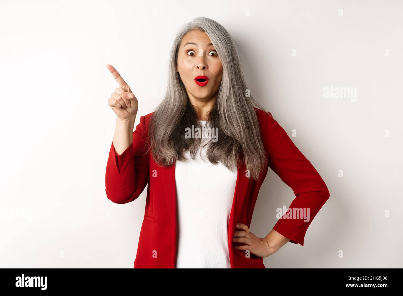 Impressed asian female entrepreneur in red blazer, pointing upper left ...
