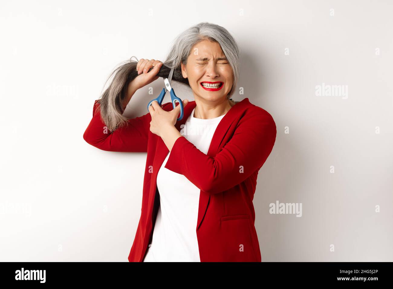 Scared asian woman cutting hair with scissors and feeling anxious ...