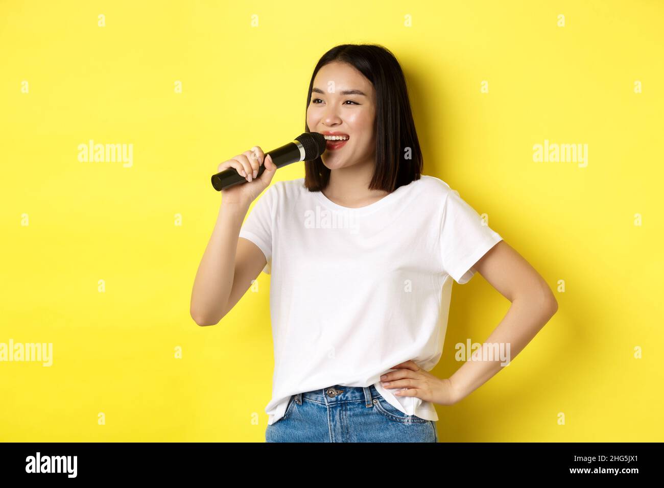 Happy asian woman singing song in karaoke, holding microphone and ...