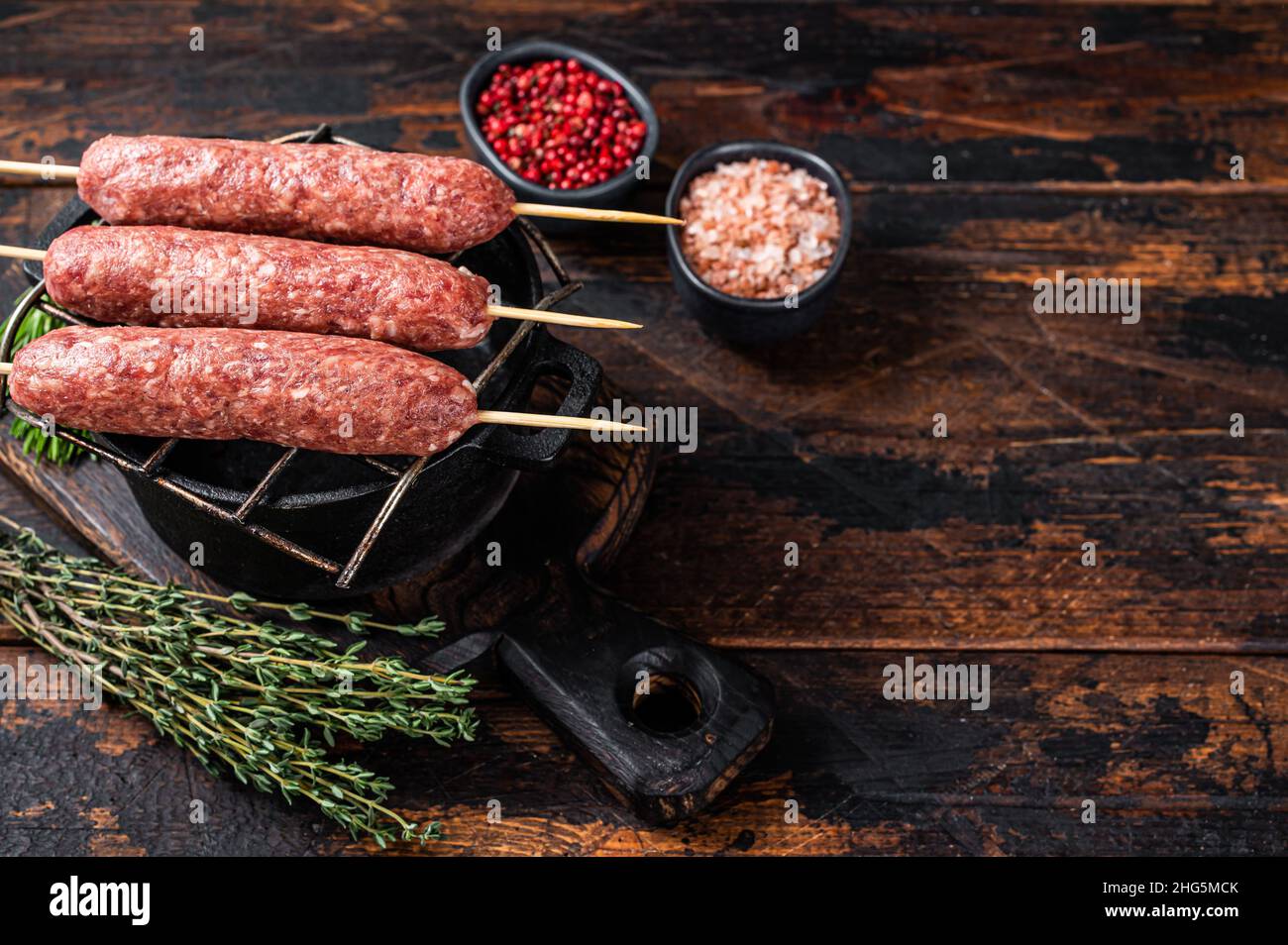 Raw kofta or lula kebabs skewers on a grill with herbs. Dark wooden ...