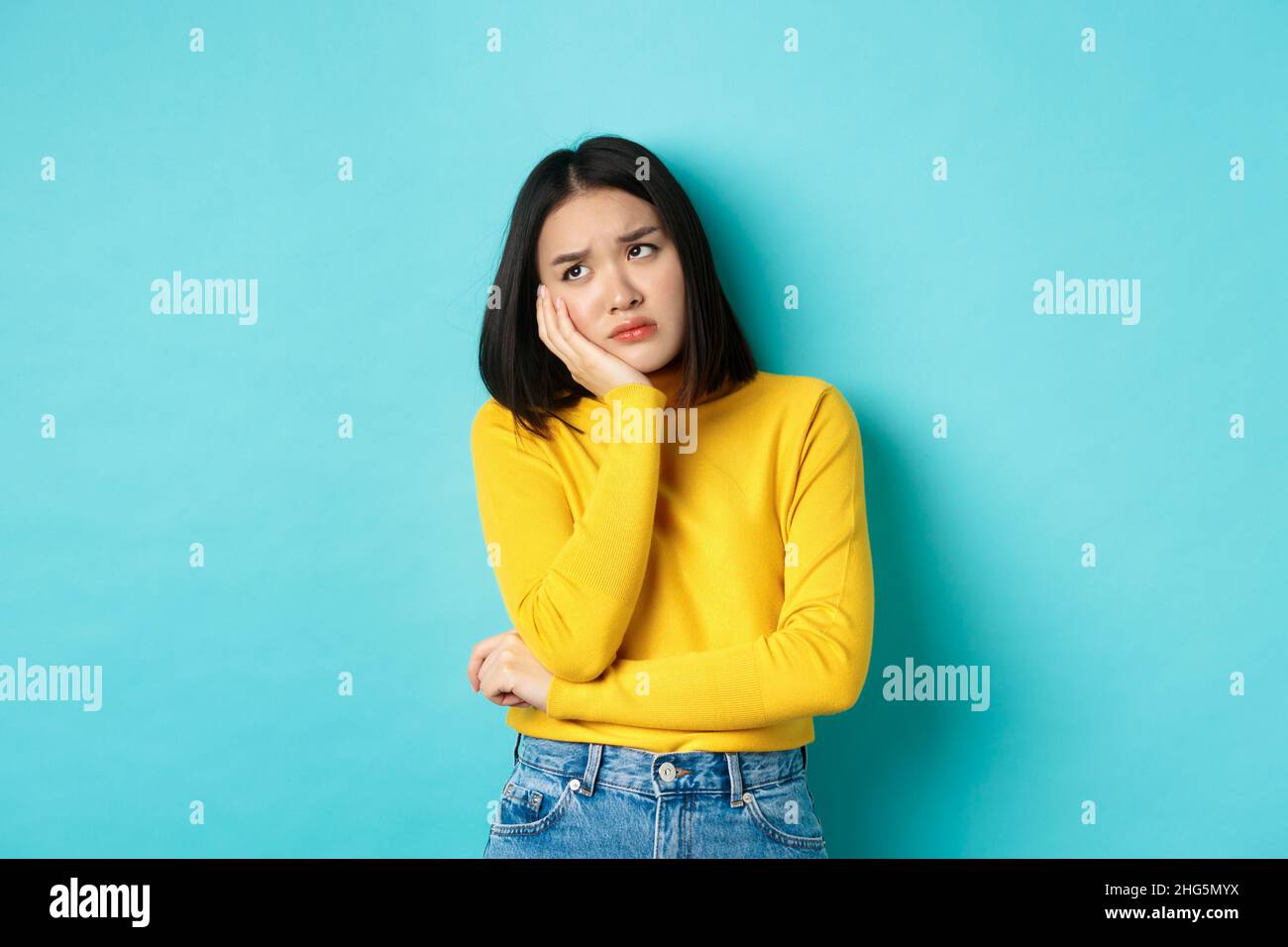 Sad and bored asian teenage girl leaning on palm, looking at upper left ...