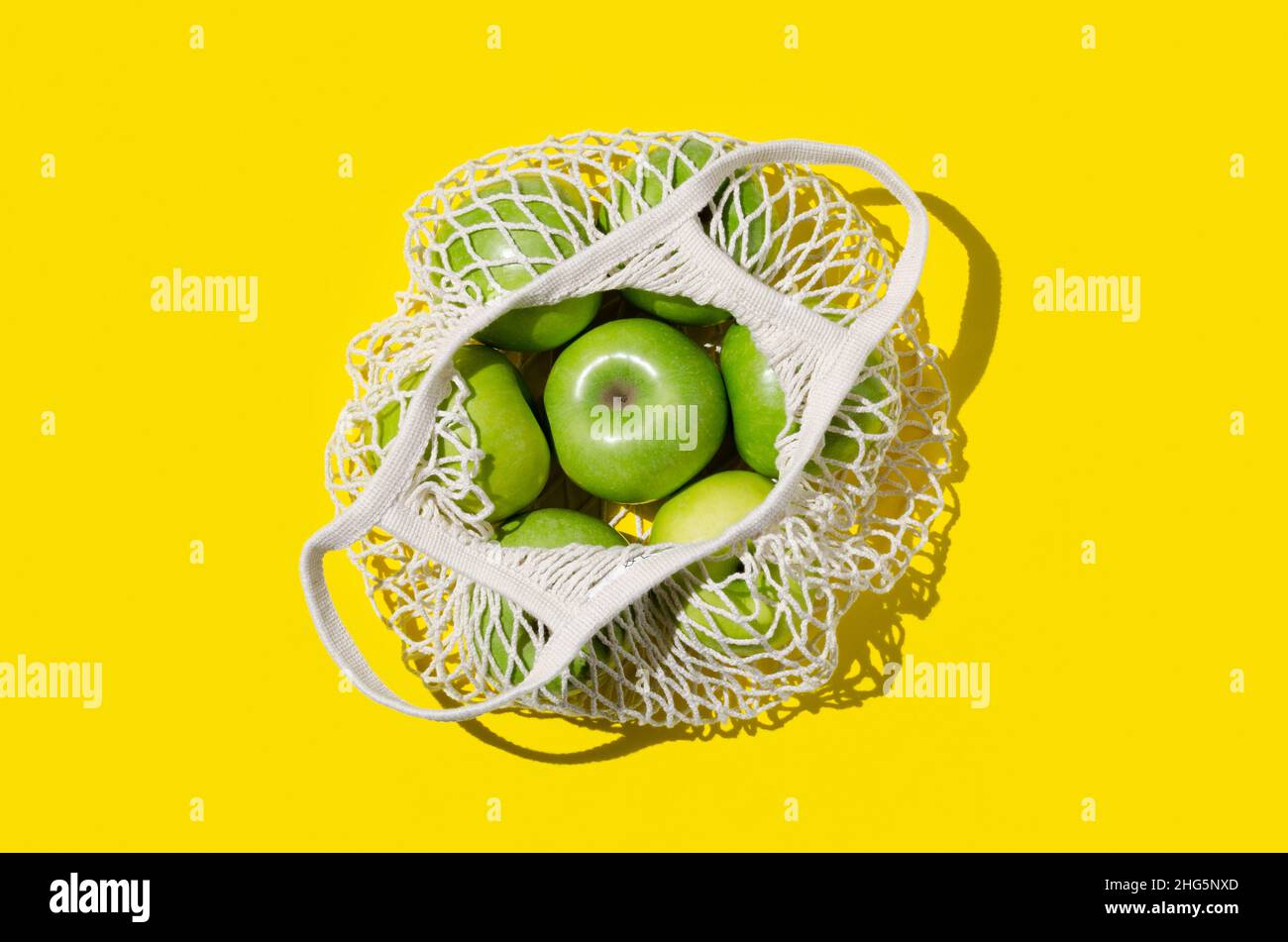 Green apples in a reusable mesh bag on a bright yellow background. Zero ...