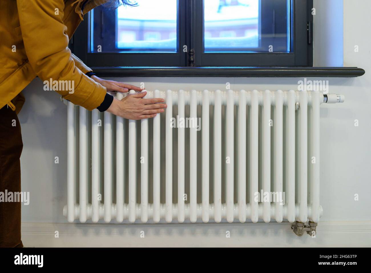Woman warming hands near heating radiator after winter walk, female checking battery temperature ...