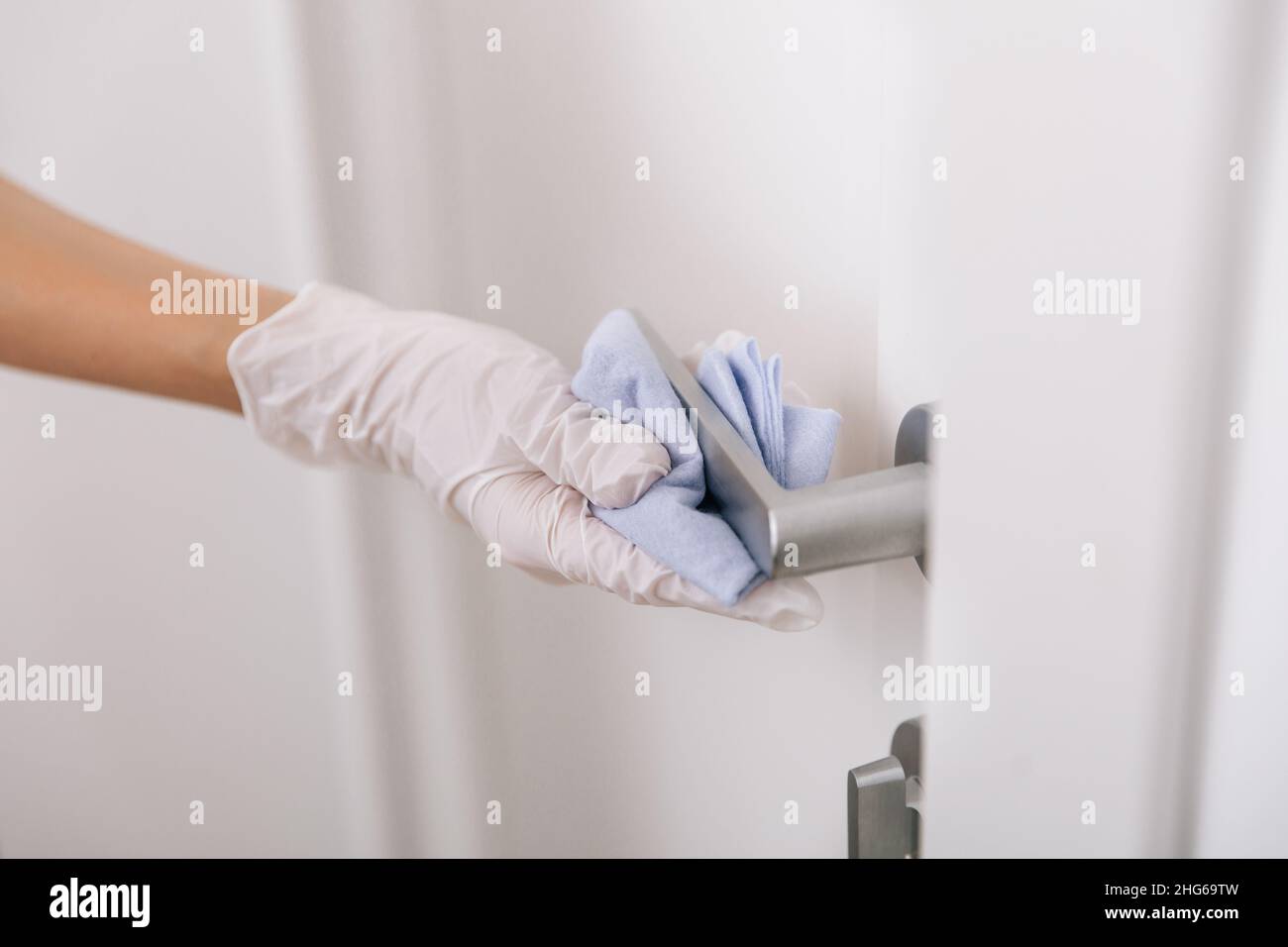 Cleaning door handle with blue wipe in white gloves. Woman hand using ...