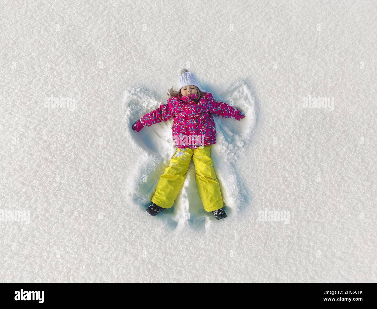 Little girl in winter clothes making angels in the snow Stock Photo - Alamy