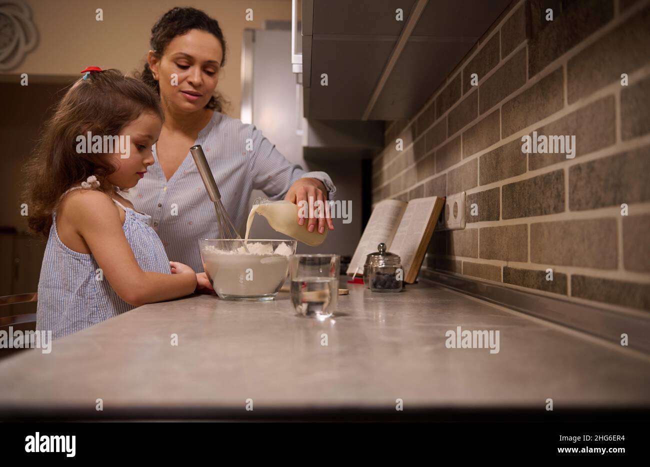 Lifestyle portrait of a mom pouring milk into bowl of flour and mixing ...