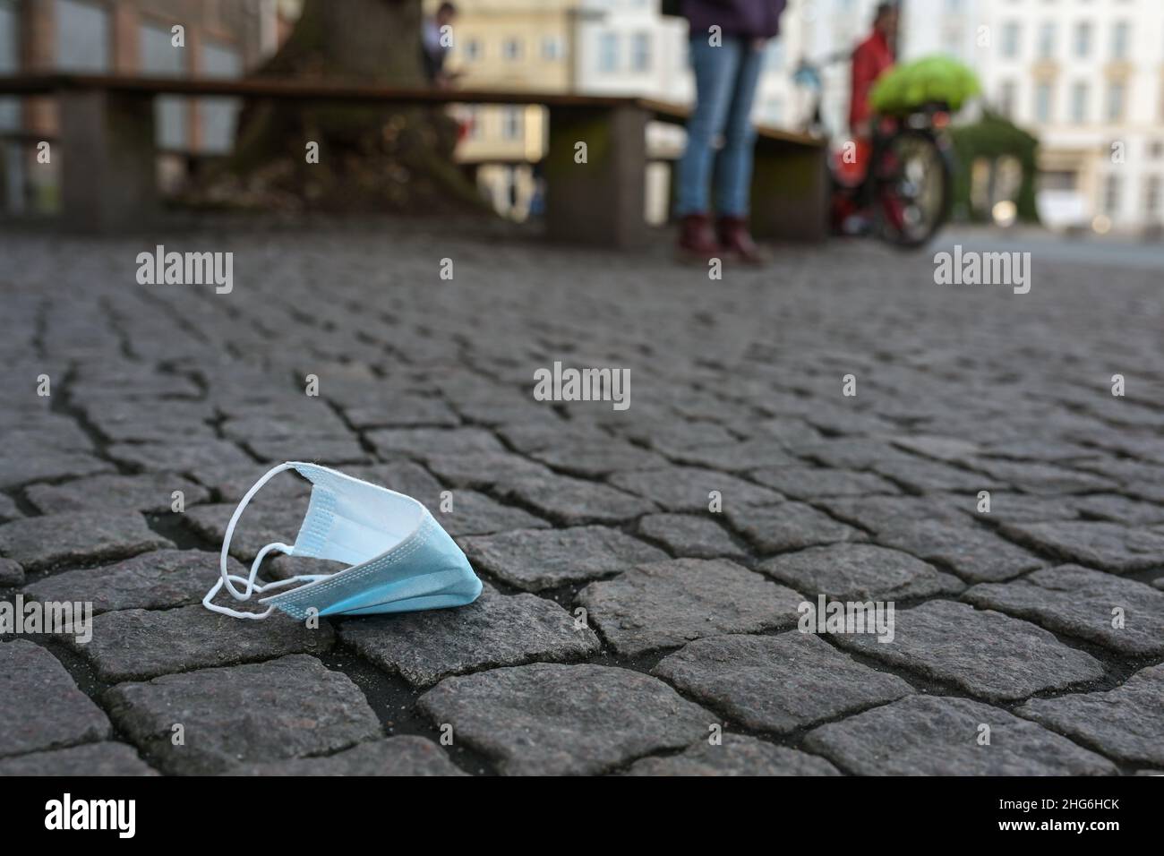 Littered surgical mask lying on a cobblestone city street, an ...