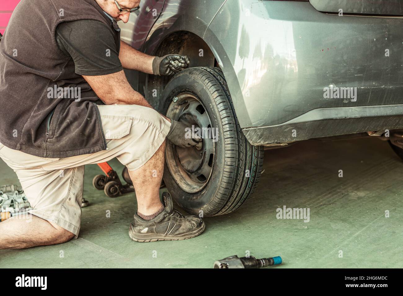 Man crouching while putting on a wheel from a car in a workshop Stock ...