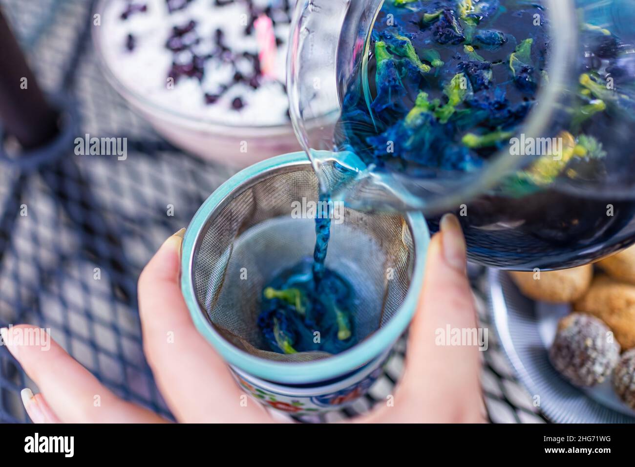 Hand pouring tea from glass teapot of butterfly pea Clitoria ternatea ...