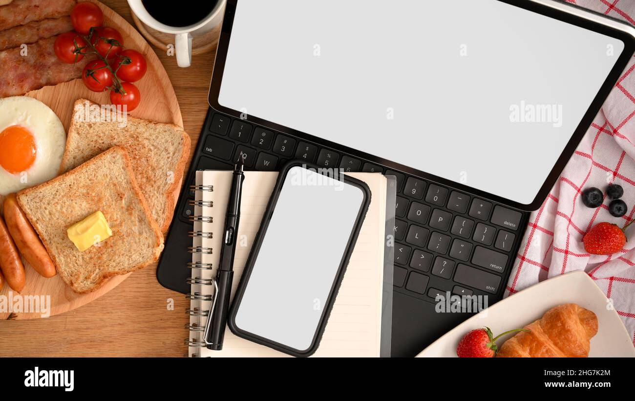 A workspace with a breakfast set concept. Smartphone and tablet blank ...