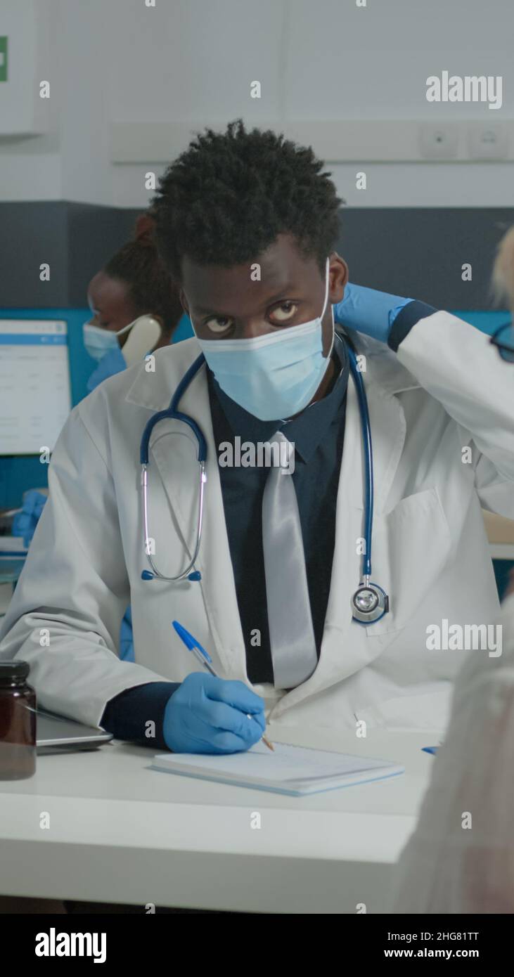 Medic with white coat sitting at desk while talking to elder woman in ...