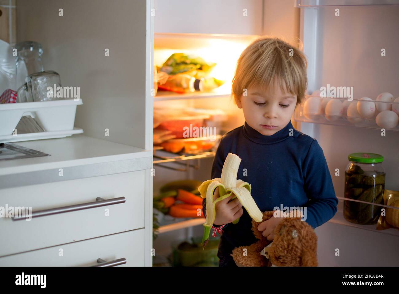 Cute toddler blond child, opening the fridge door and taking fruits and ...
