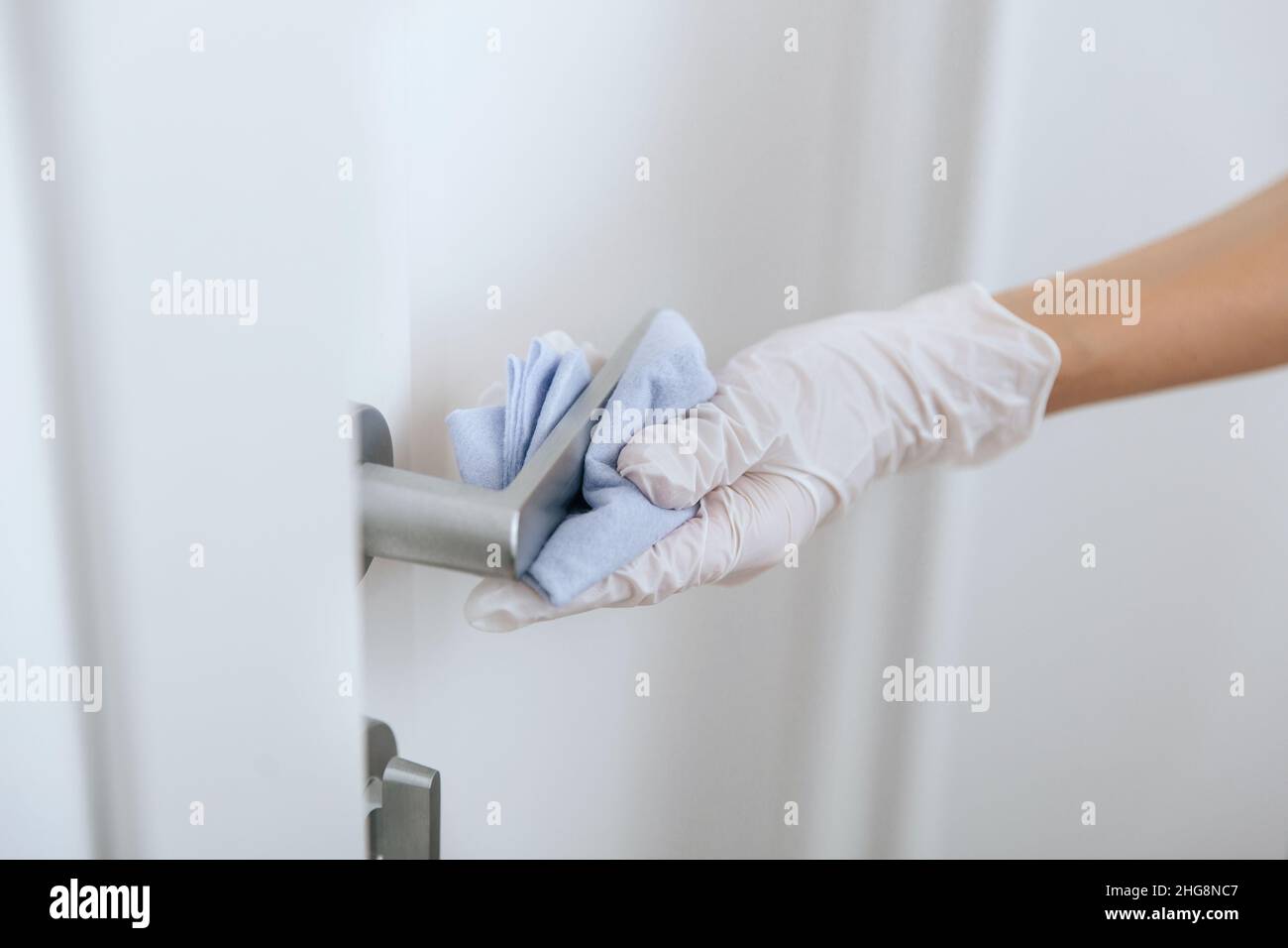 Cleaning door handle with blue wipe in white gloves. Sanitize surfaces ...