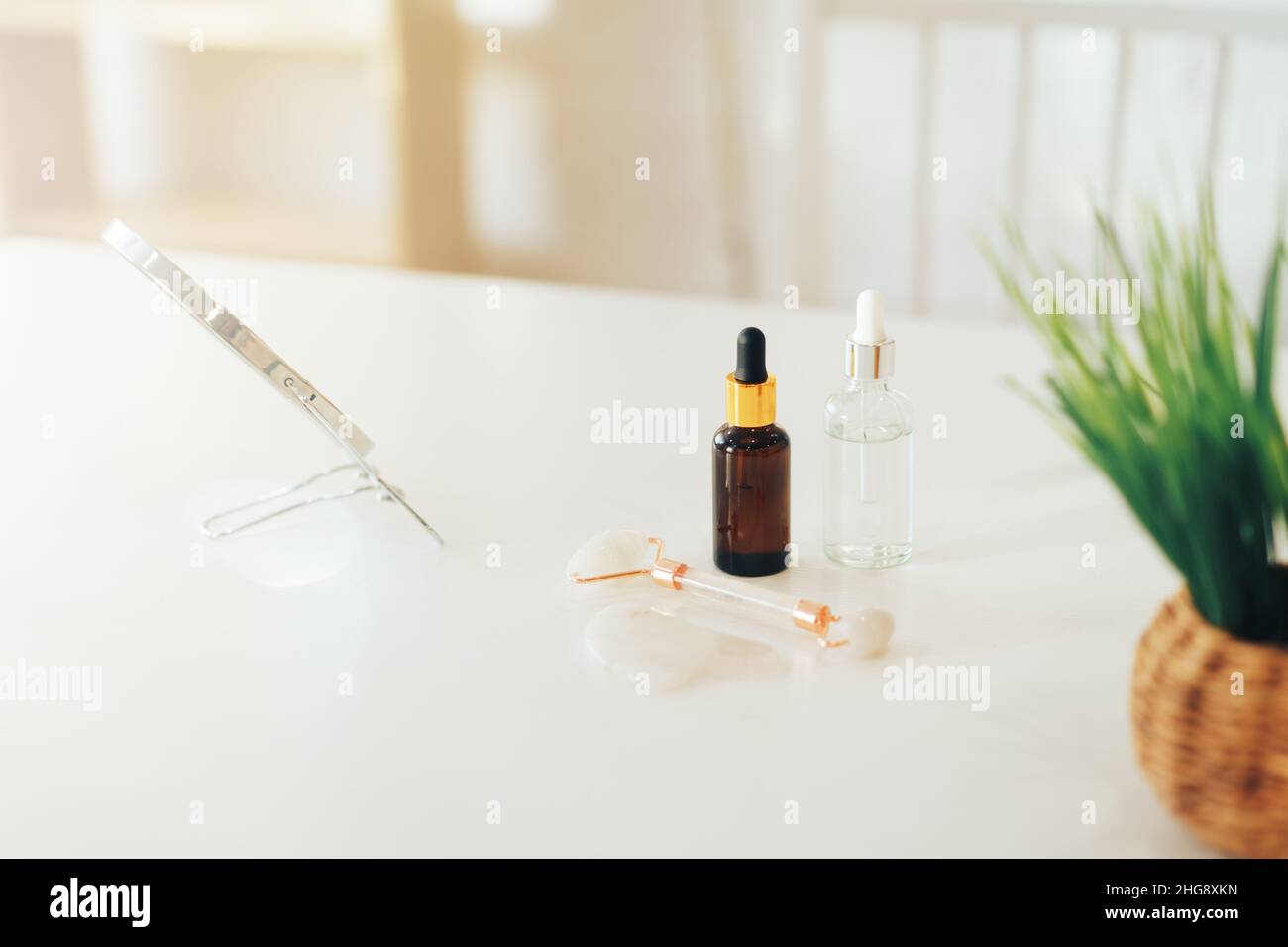 Glass vials with pipette and massage roller next to mirror and grass on ...