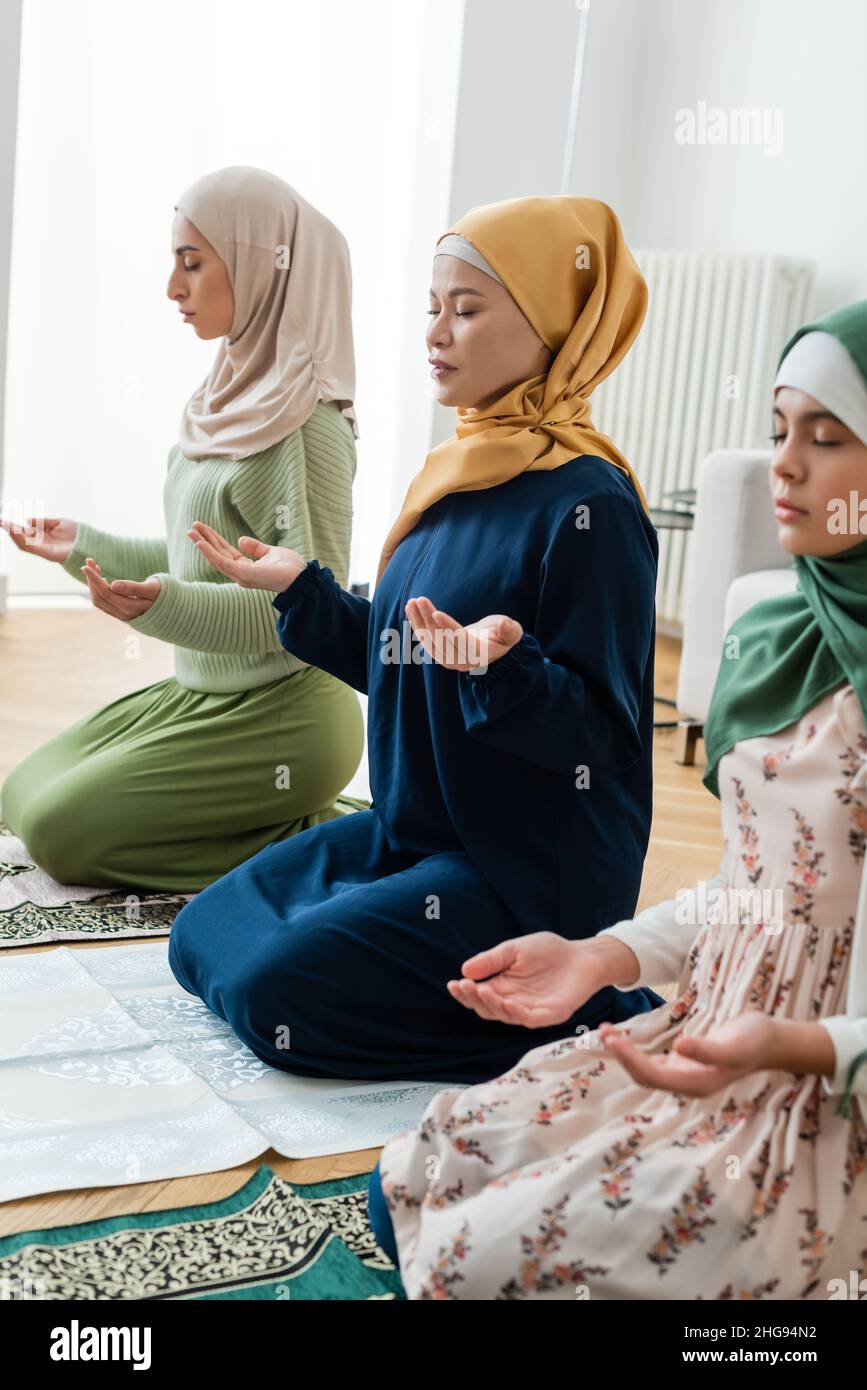 Asian woman in traditional muslim clothes praying near arabian daughter and granddaughter at ...