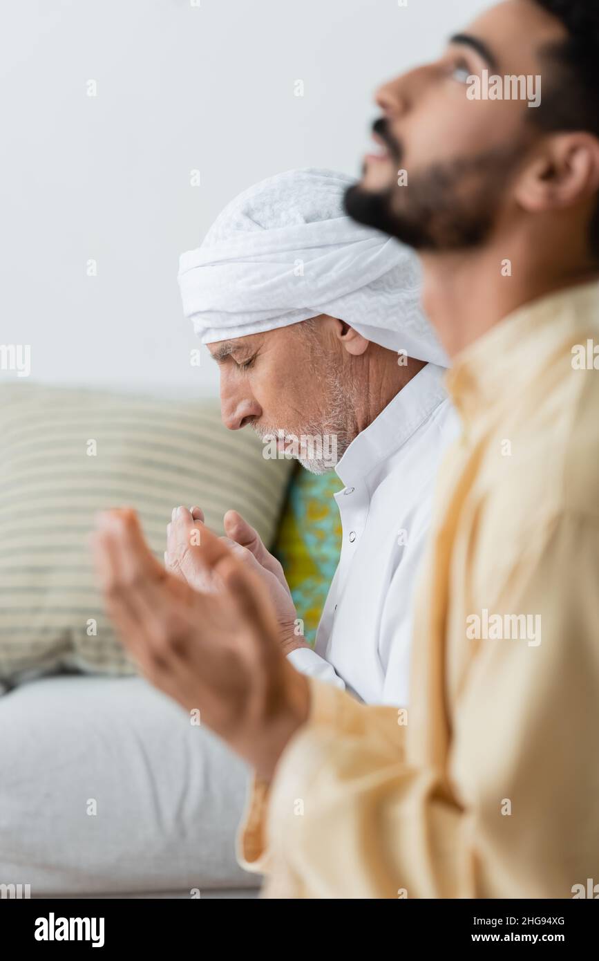 Side view of mature man praying with closed eyes near blurred arabian ...