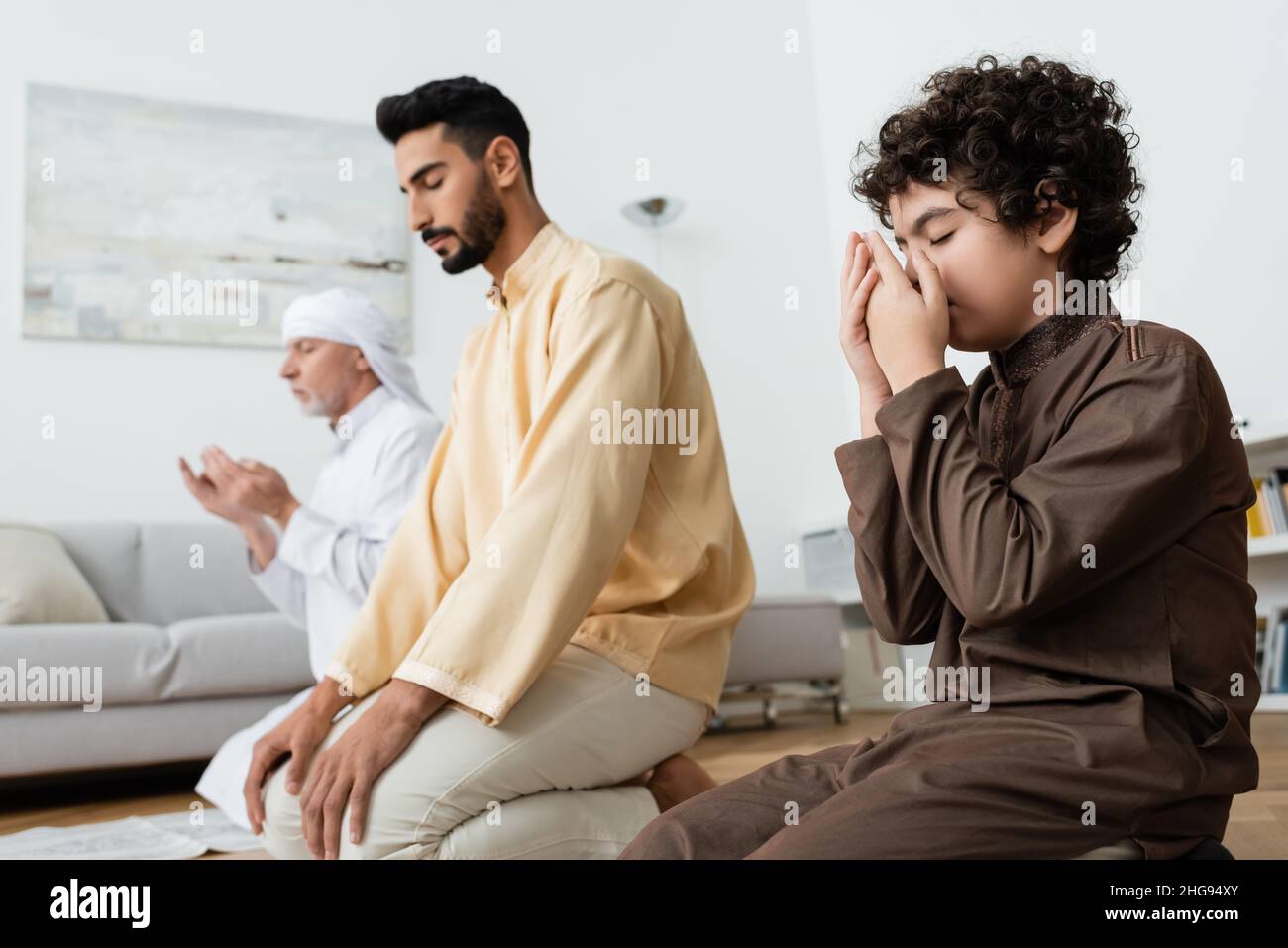 Muslim boy holding hands near face while praying near multiethnic family at home Stock Photo - Alamy
