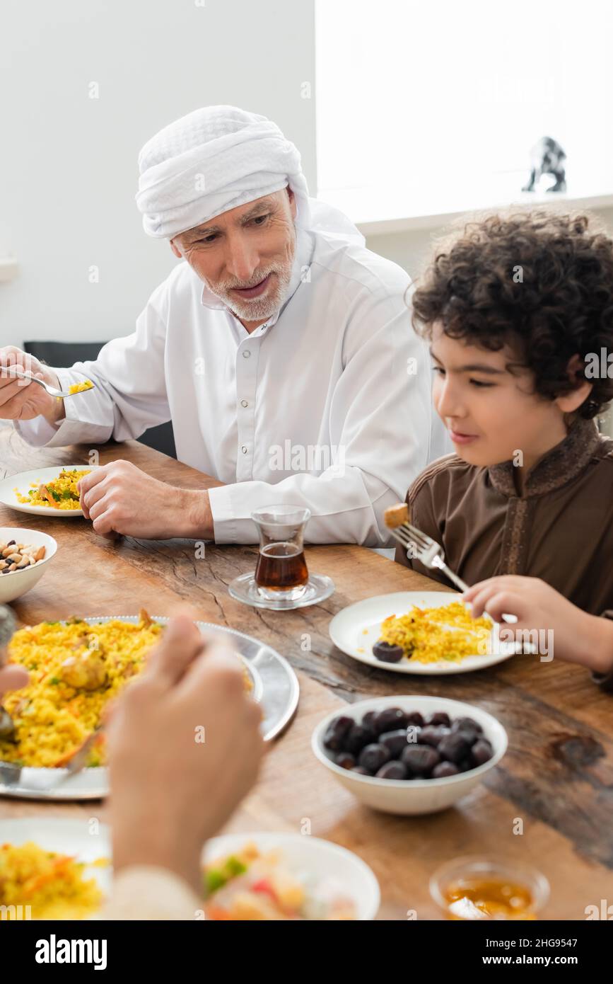 muslim man eating pilaf with arabian grandson during family dinner ...