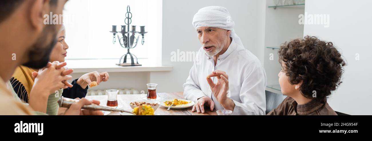 mature muslim man gesturing while talking during dinner with ...