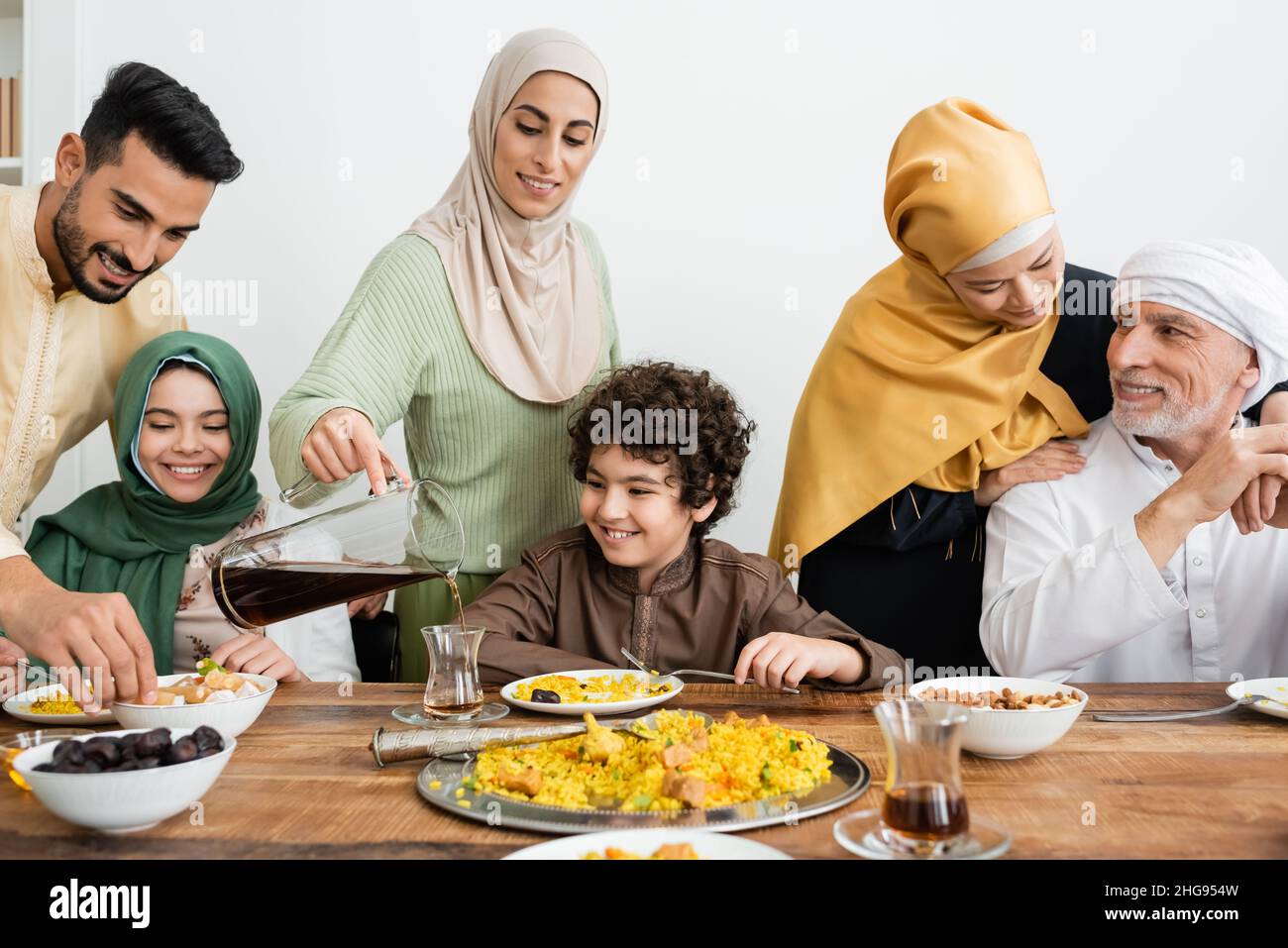arabian woman pouring tea near happy multiethnic muslim family having ...