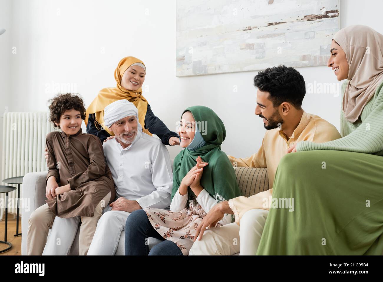 happy multicultural muslim family looking at smiling girl while sitting ...
