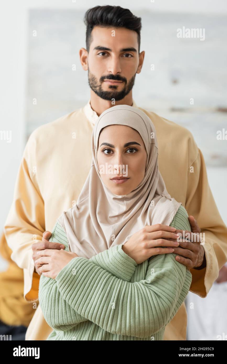 young arabian couple in traditional clothes looking at camera at home ...