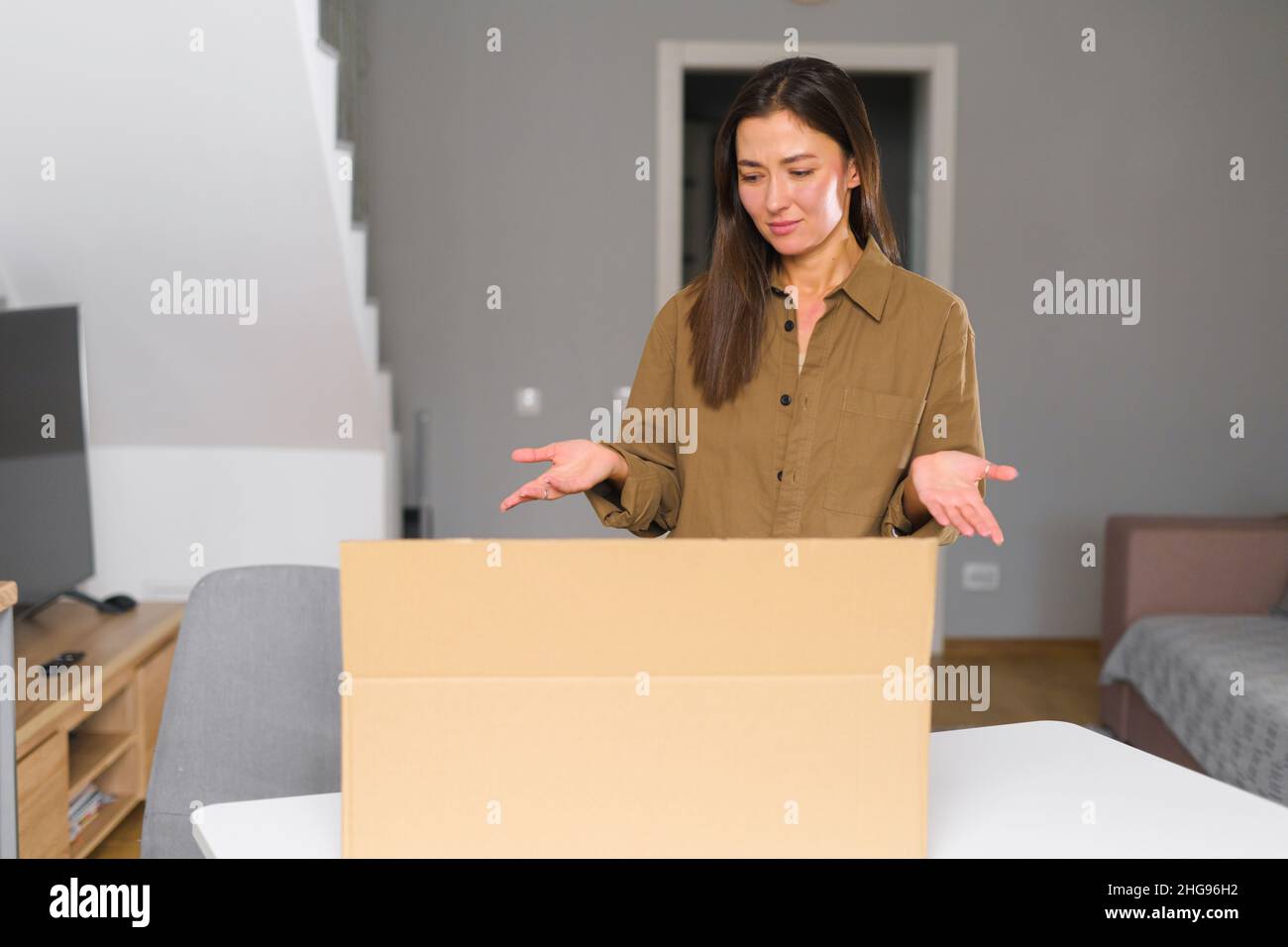 Attractive woman unpack the box in the living room and feeling sad ...