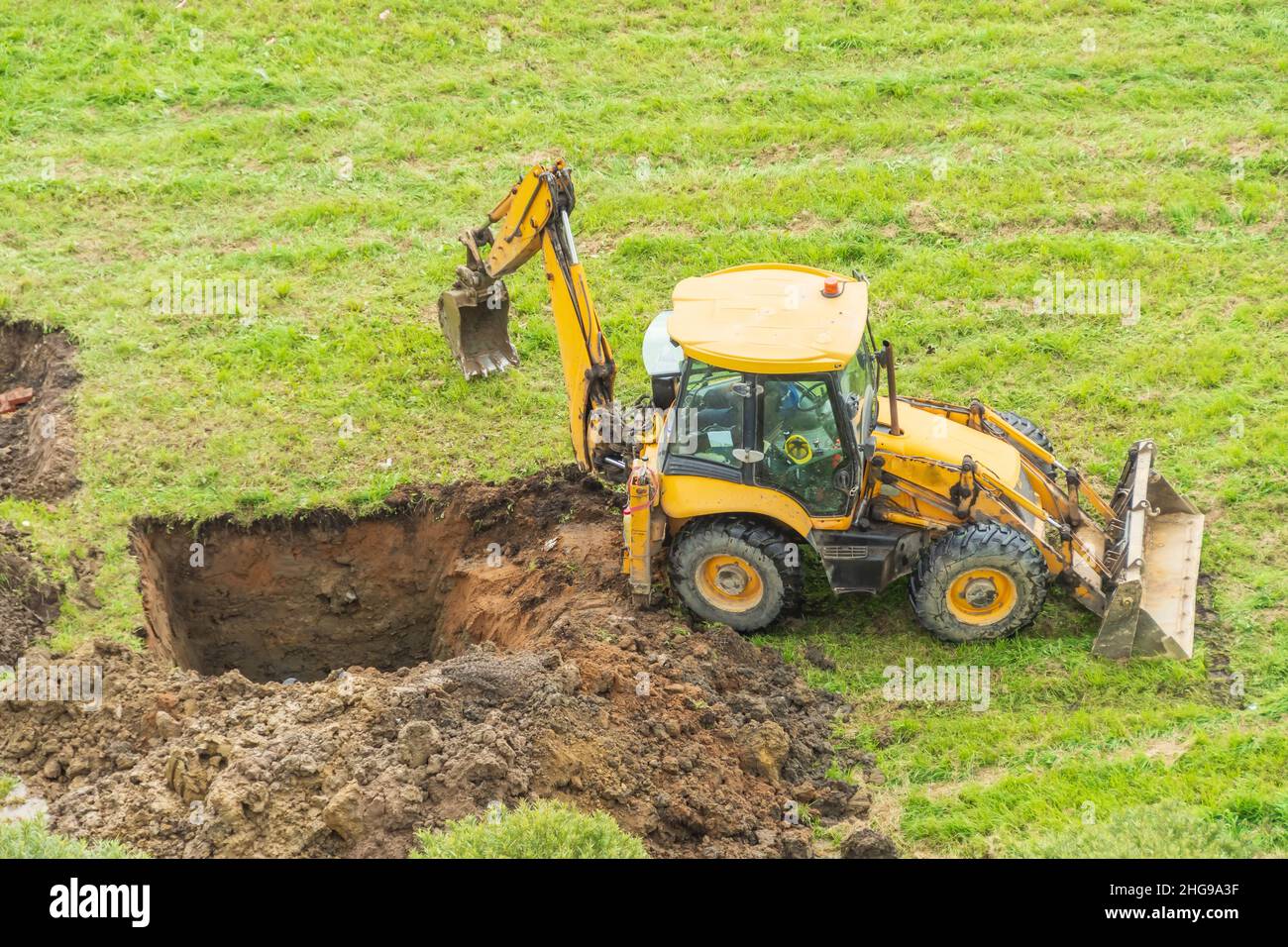 Tractor excavator digs a hole for installing a collector line and pipes ...