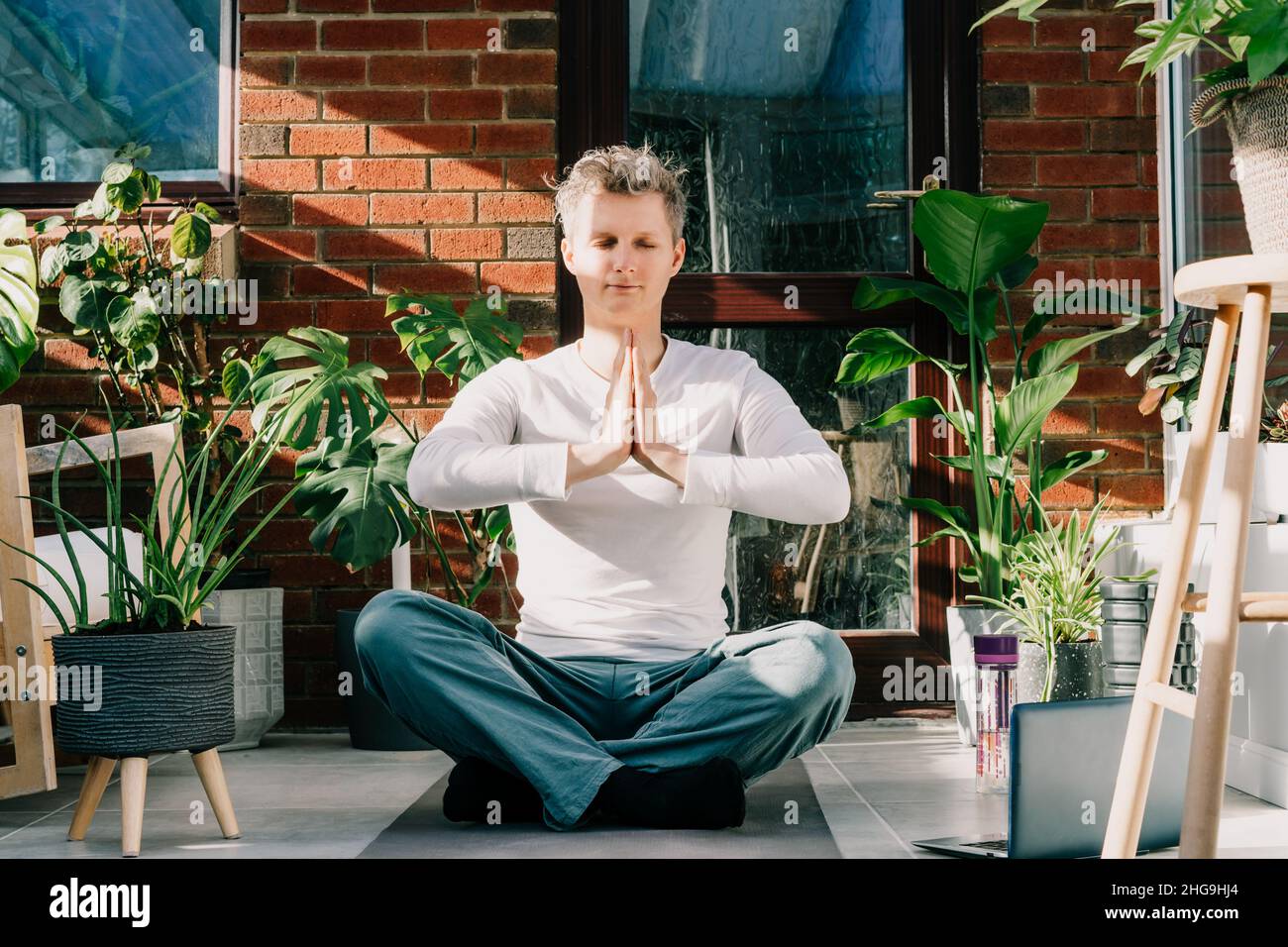 Young man doing yoga position Namaste in cozy loft style room full of ...