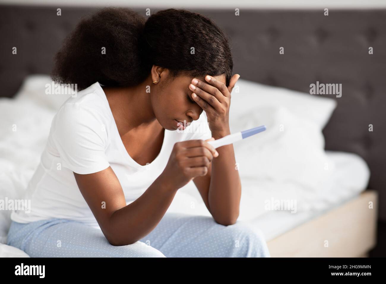 Upset African American Woman Sitting On Bed With Pregnancy Test Stock