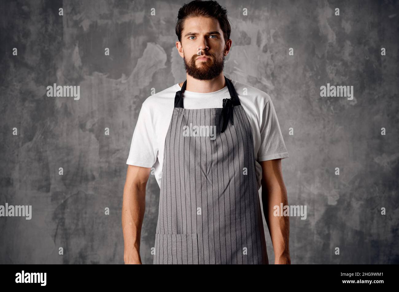 confident hairdresser in an apron with a comb and scissors in his hands ...