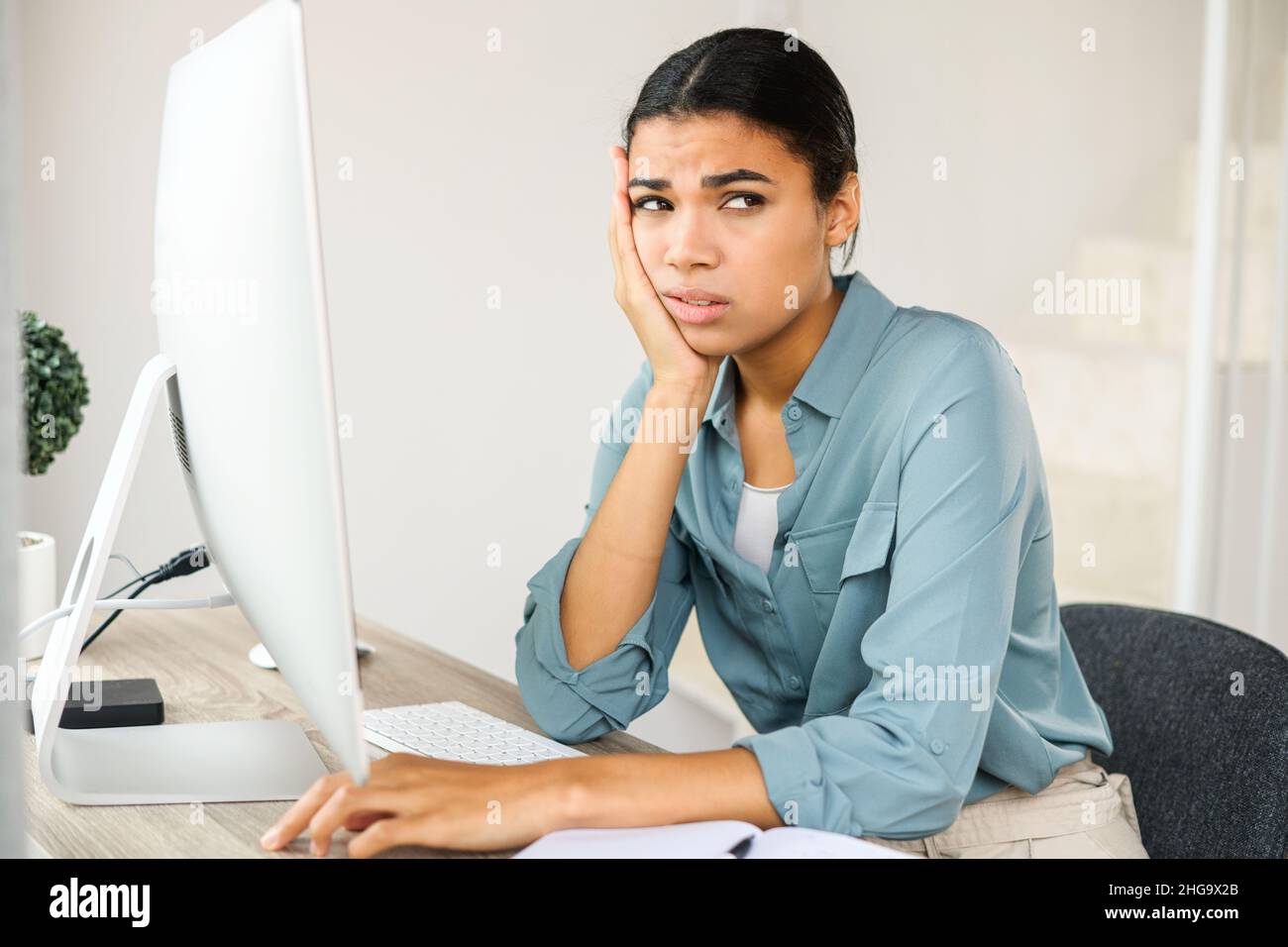 Multiracial young woman is tired, looking away in front of the computer ...