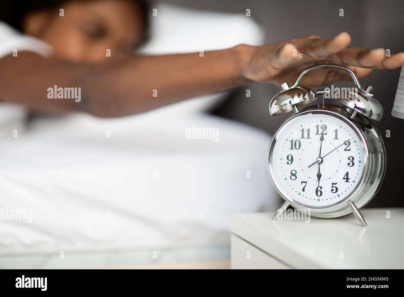 Black woman laying in bed, turning off alarm on bedside Stock Photo - Alamy
