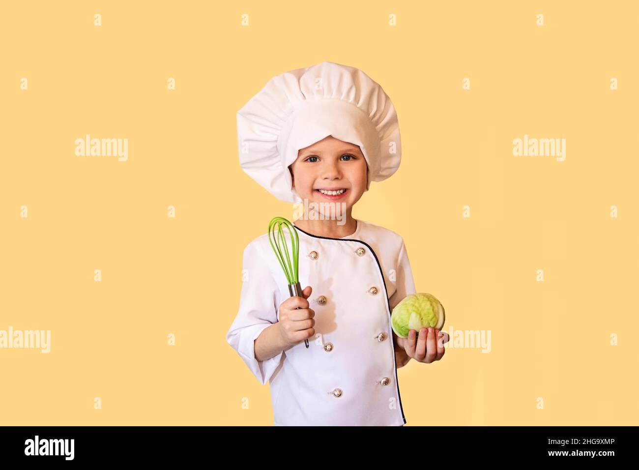 Smiling child in white chef uniform,holding a cabbage and a whisk in ...